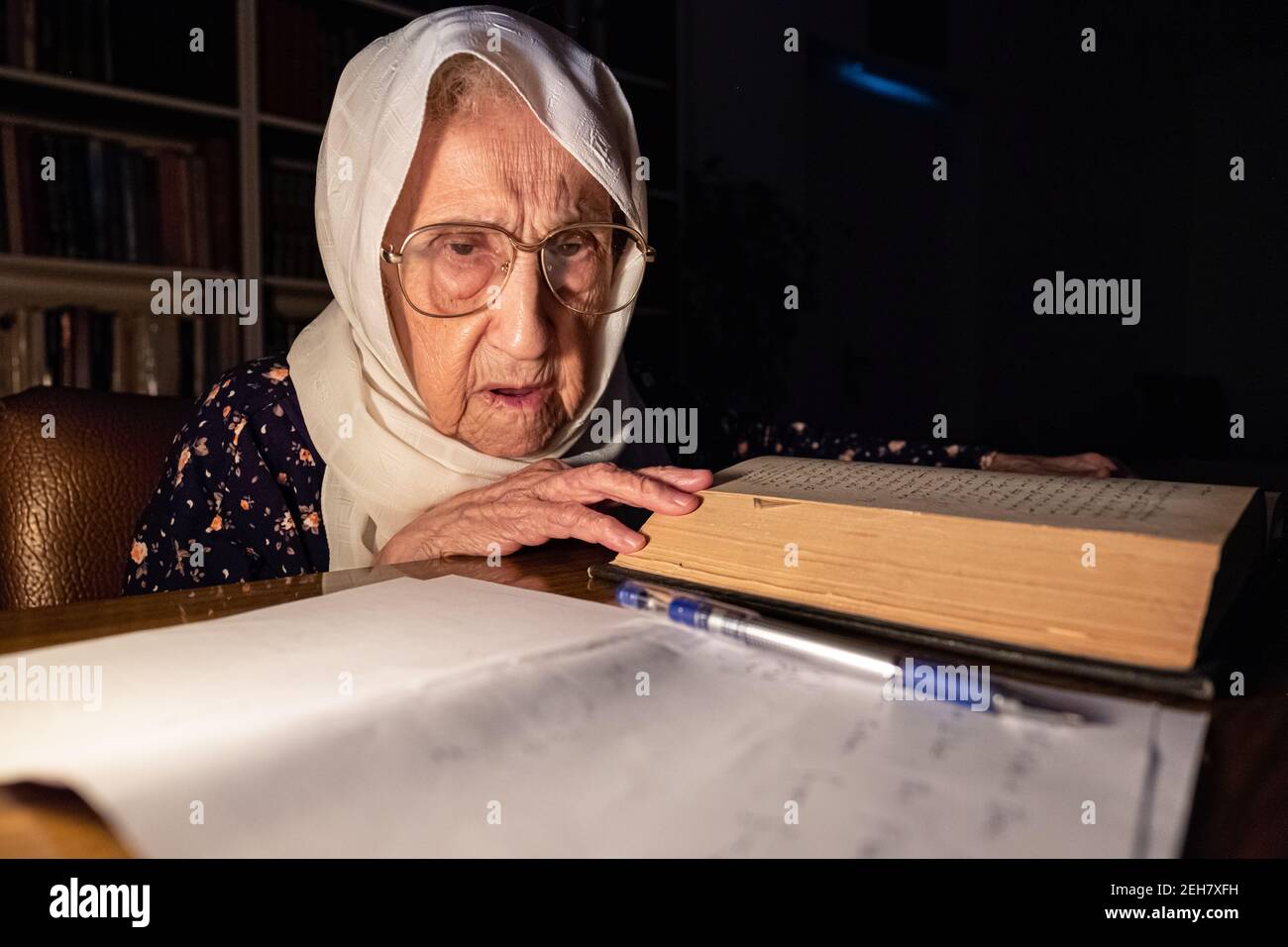 Old lady reading books in dark room with candles light and writing down ...