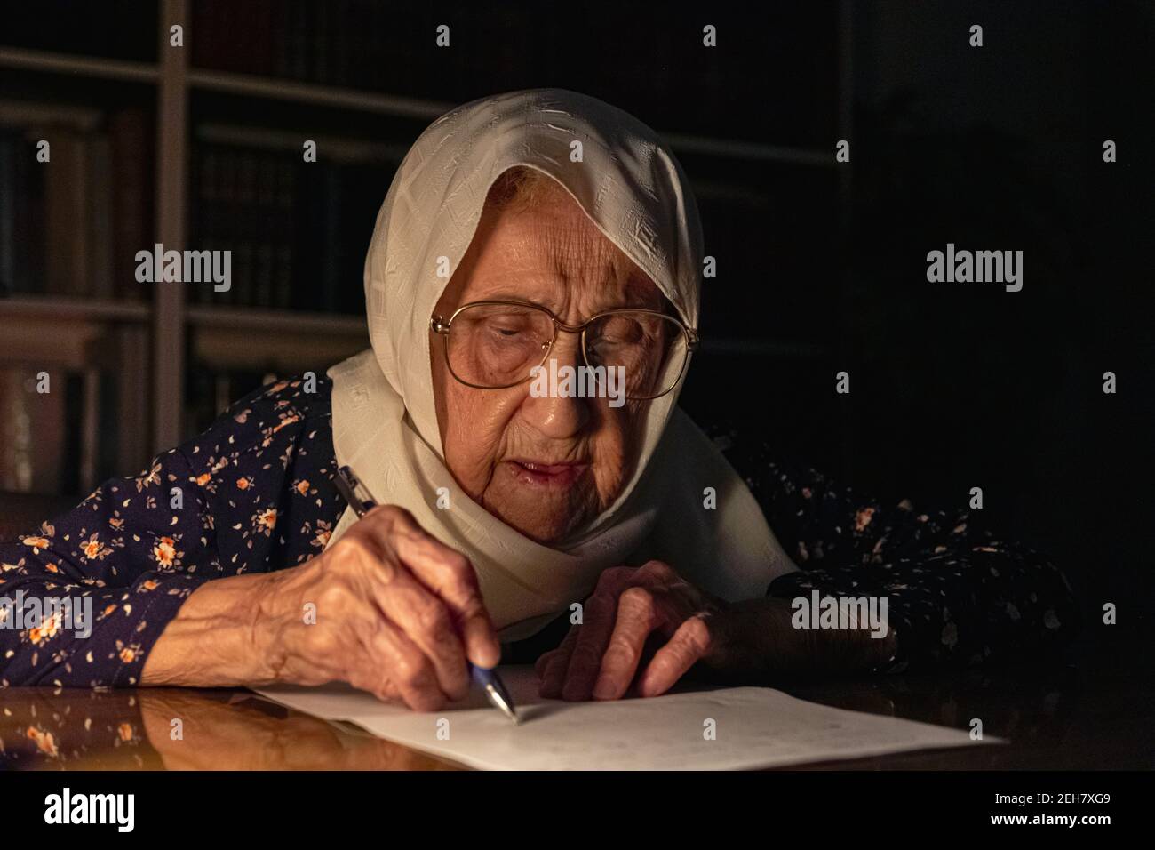 Old lady reading books in dark room with candles light and writing down ...