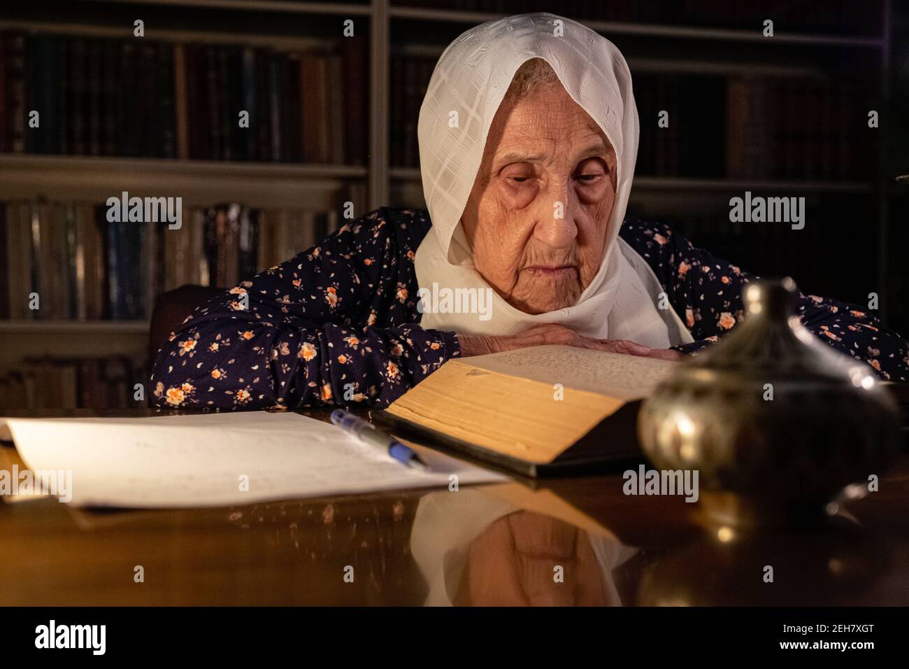 Old lady reading books in dark room with candles light and writing down ...