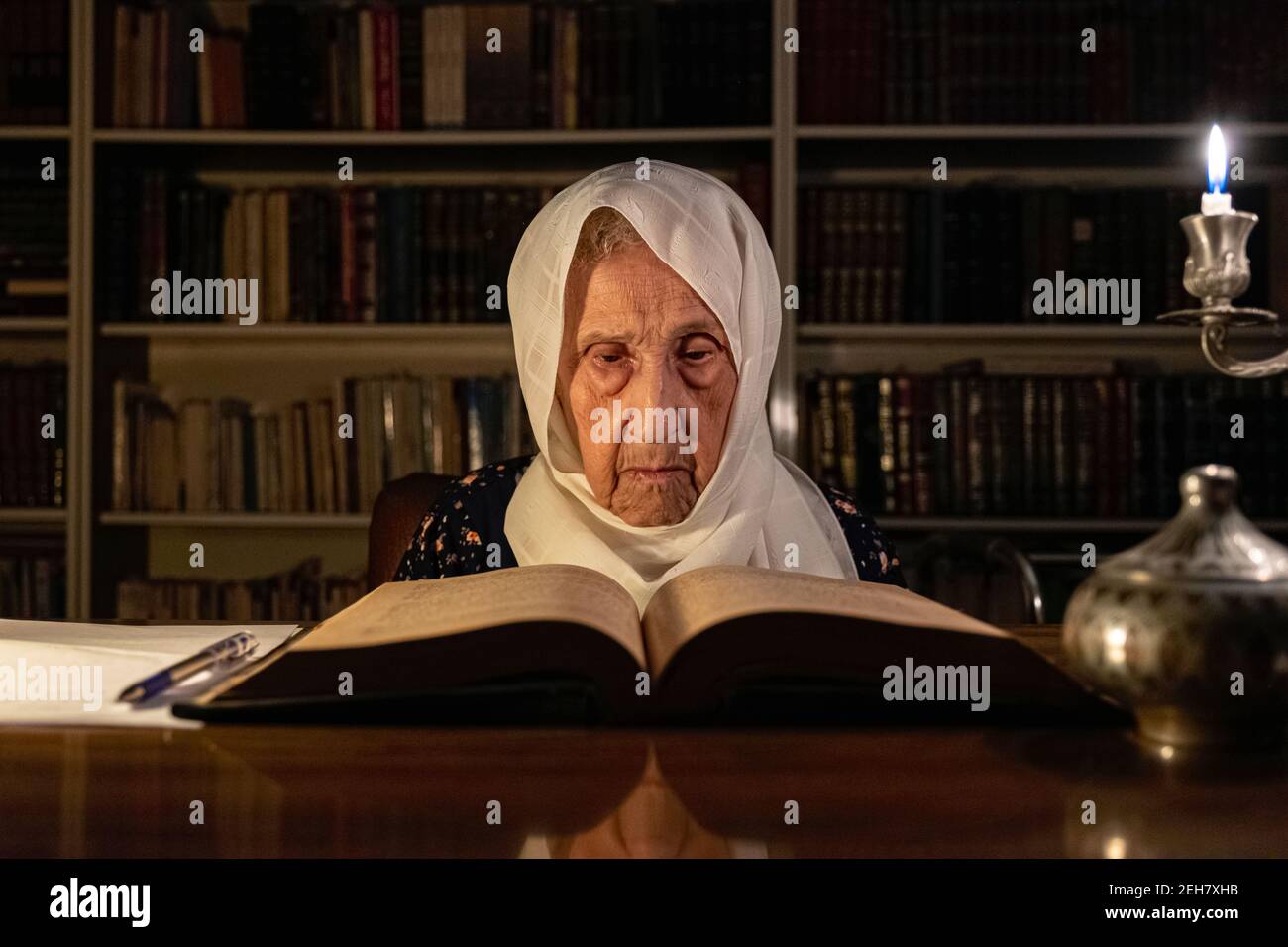 Old lady reading books in dark room with candles light and writing down ...