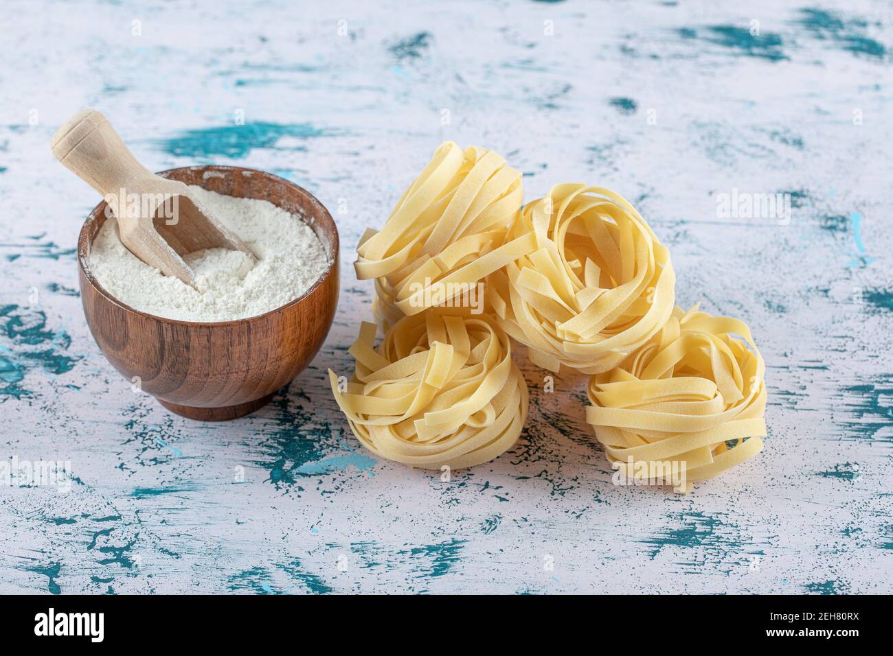 Raw tagliatelle nests and bowl of flour on colorful surface Stock Photo ...