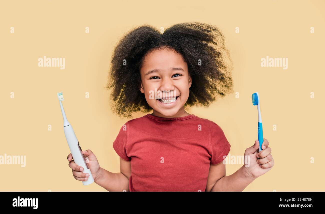 Smiling African American little girl holds manual and electric sonic ...