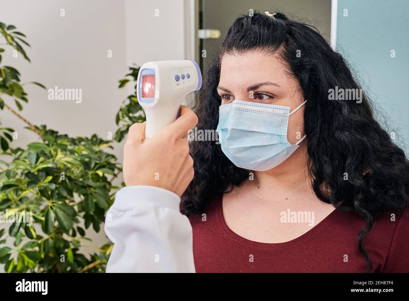Woman wearing medical mask during measuring her body temperature with ...