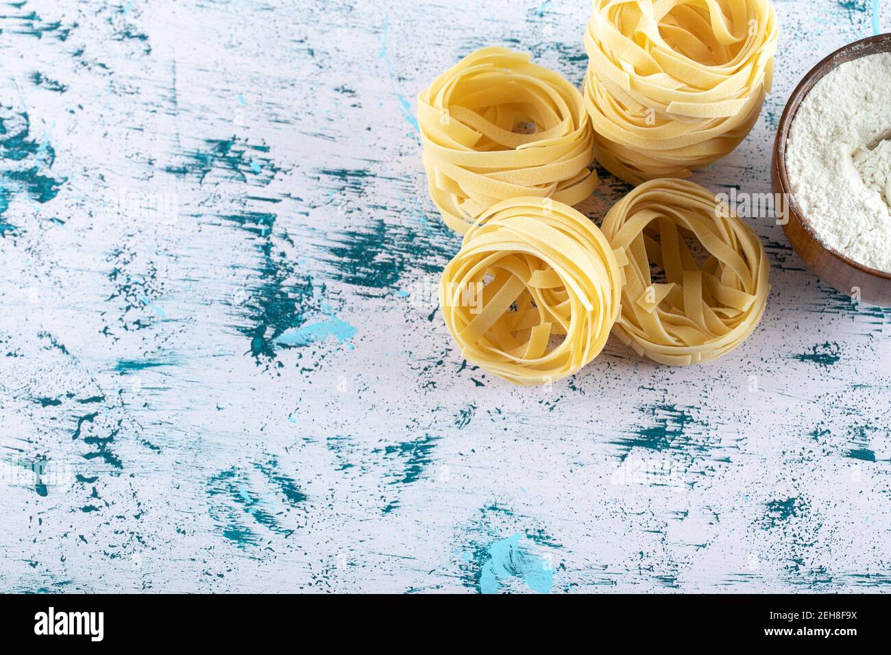 Raw tagliatelle nests and bowl of flour on colorful surface Stock Photo ...