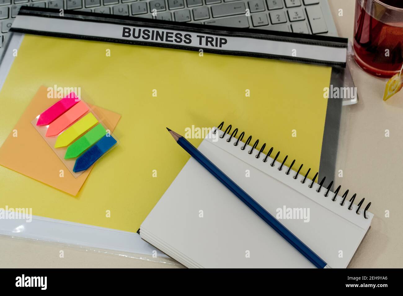 Notepad with a pencil on a yellow folder labelled "BUSINESS TRIP" on a ...