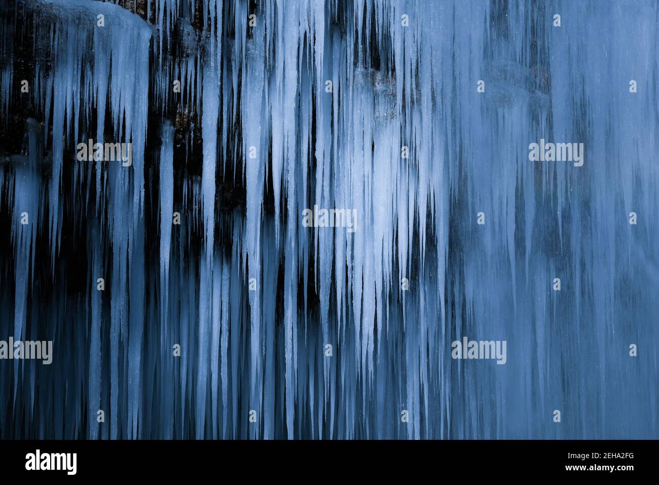 Beautiful long icicles of a frozen waterfall. Water flowing and ...