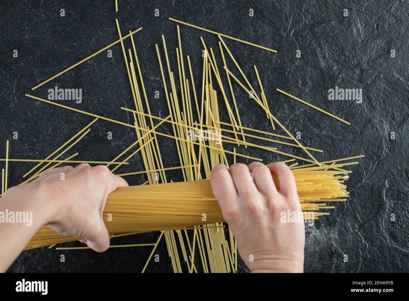 Woman hands breaking spaghetti on dark background Stock Photo - Alamy