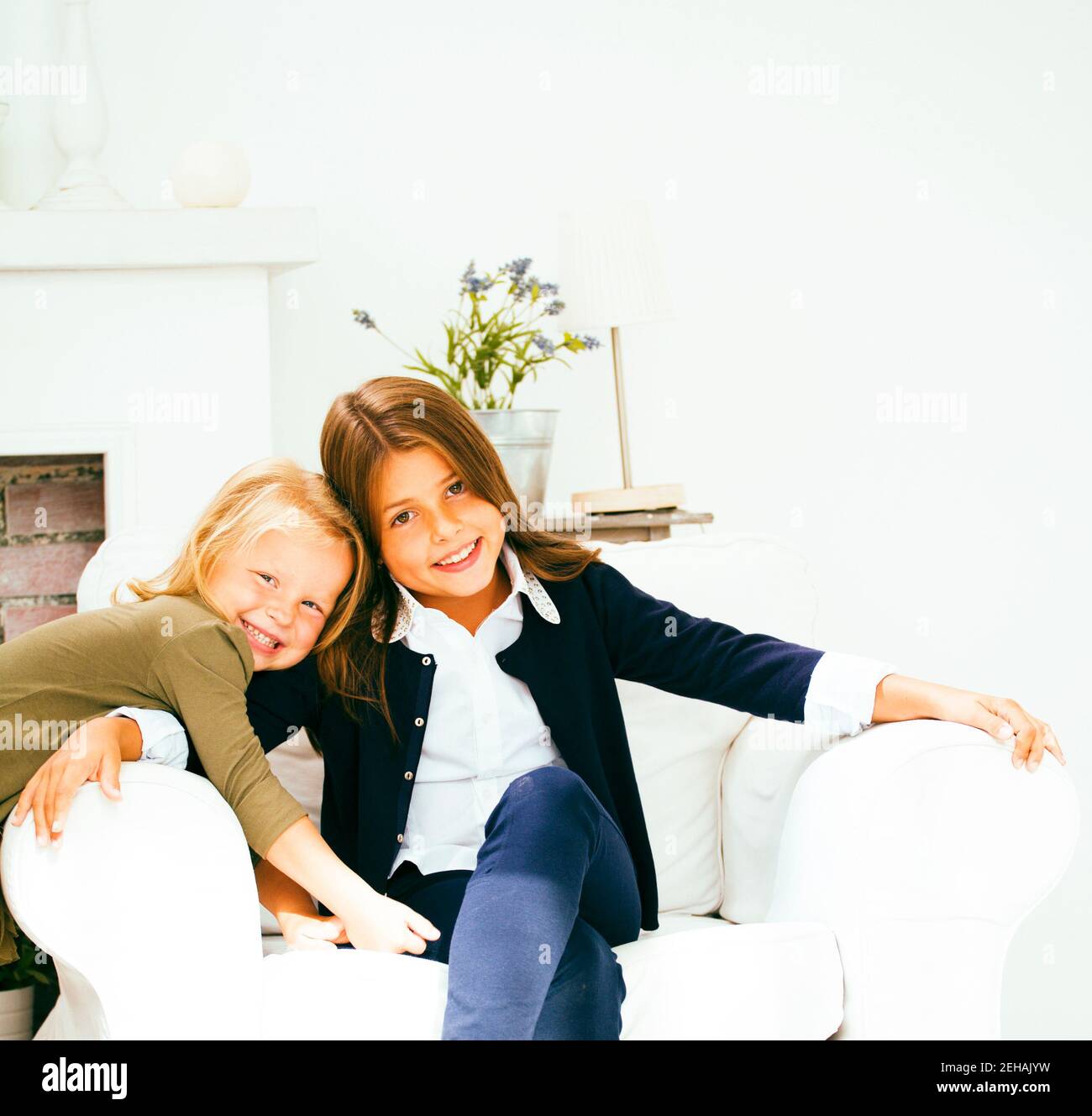 two cute sisters at home playing, little girl in house interior on sofa ...