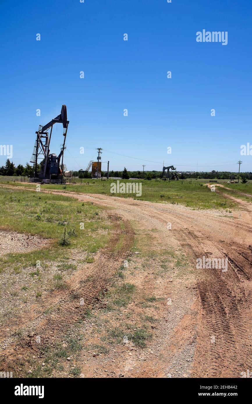 Oil rigs and old metal tanks out in field with muddy tracks leading out ...