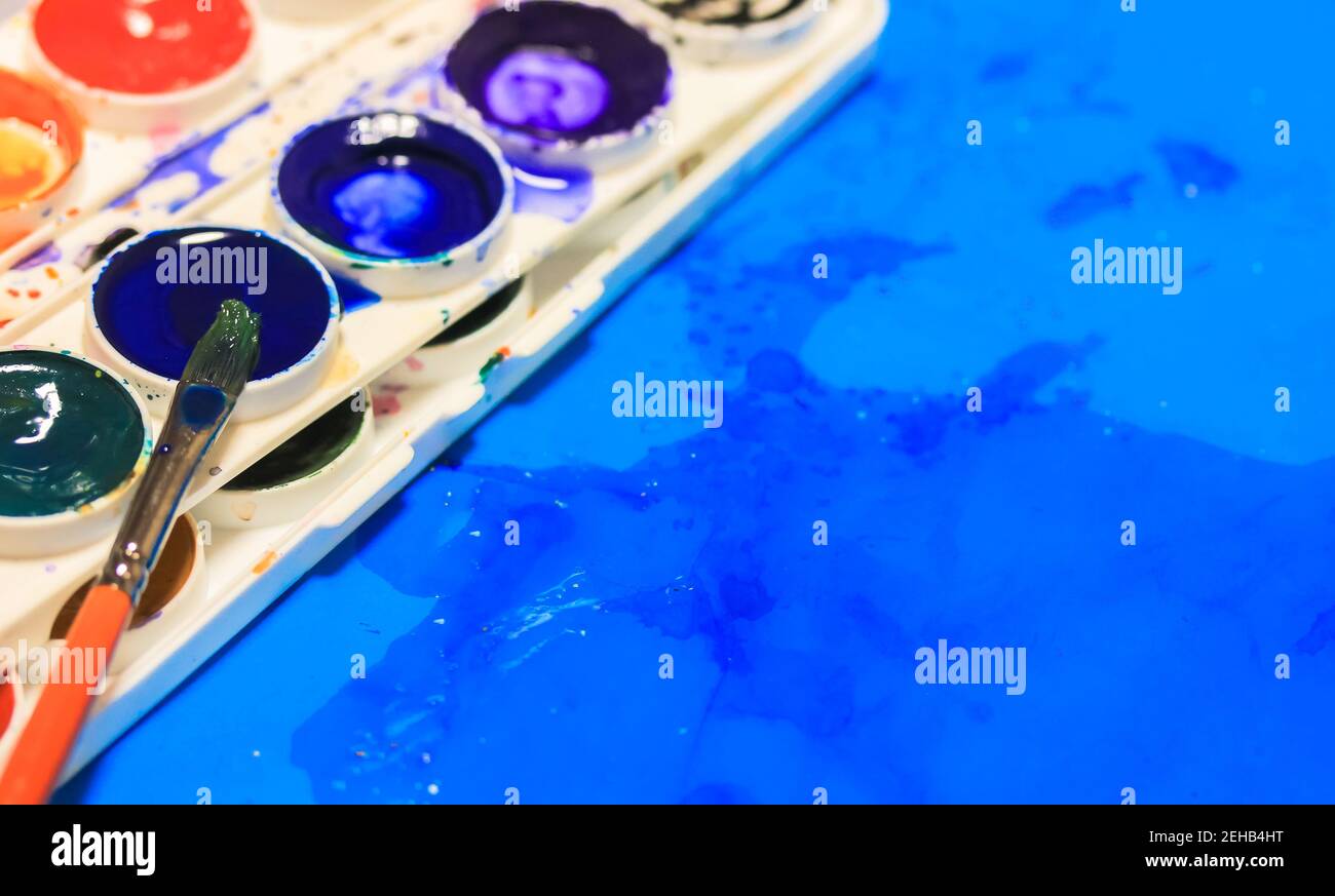 Palette with watercolors and brush on a blue desk background. Color ...