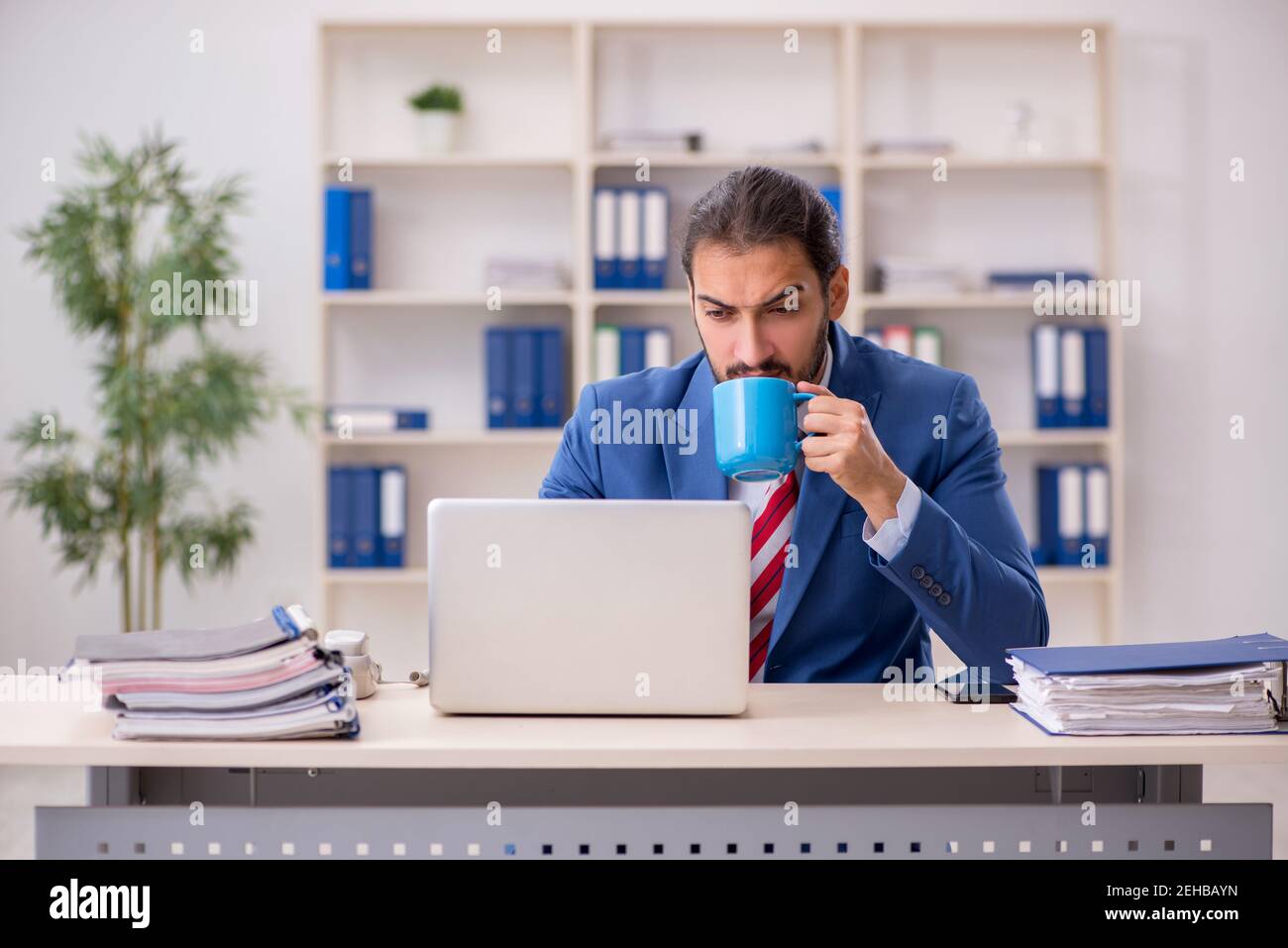 Young employee drinking coffee at workplace Stock Photo - Alamy