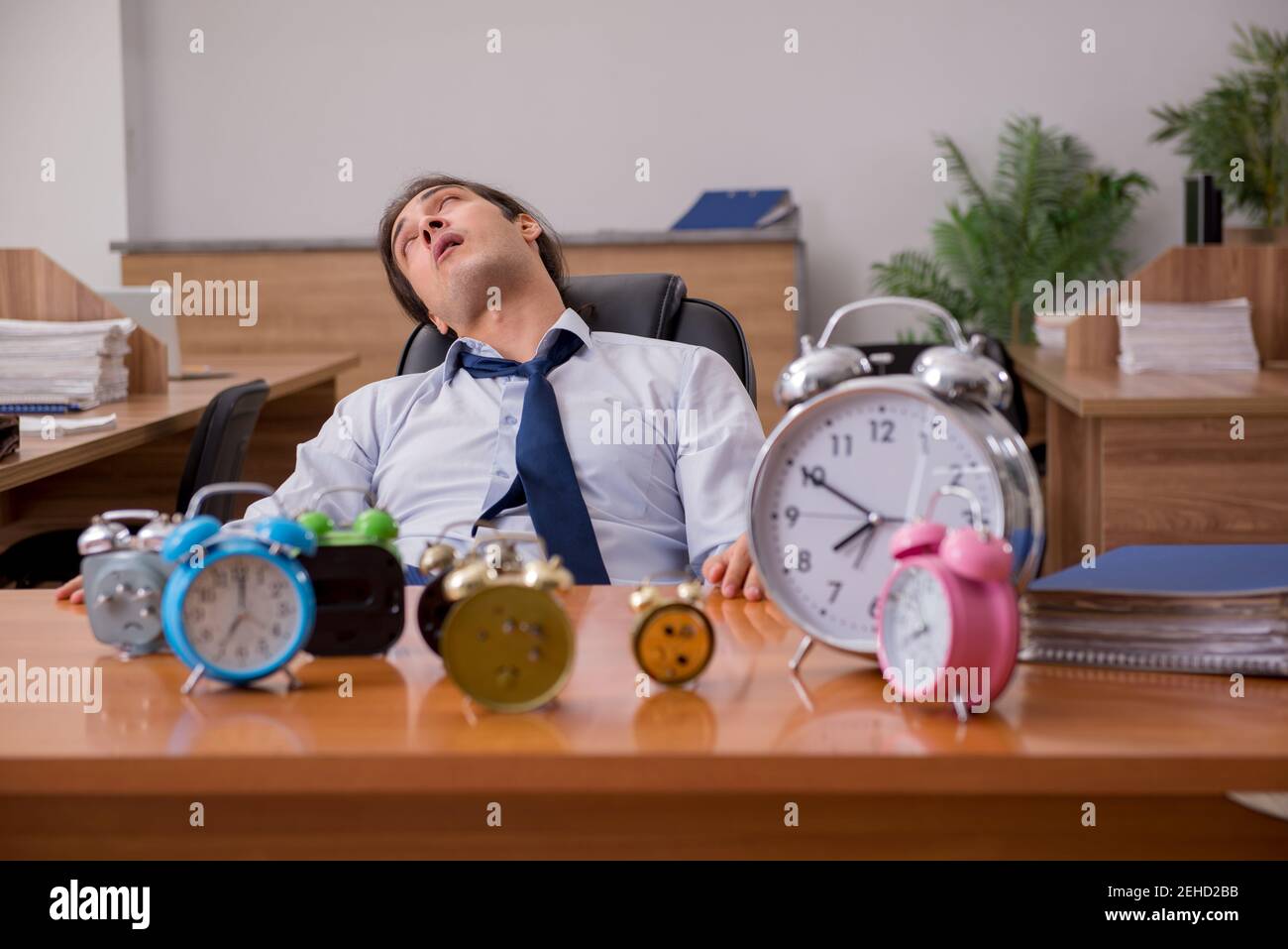 Young businessman sleeping in the office in time management concept ...