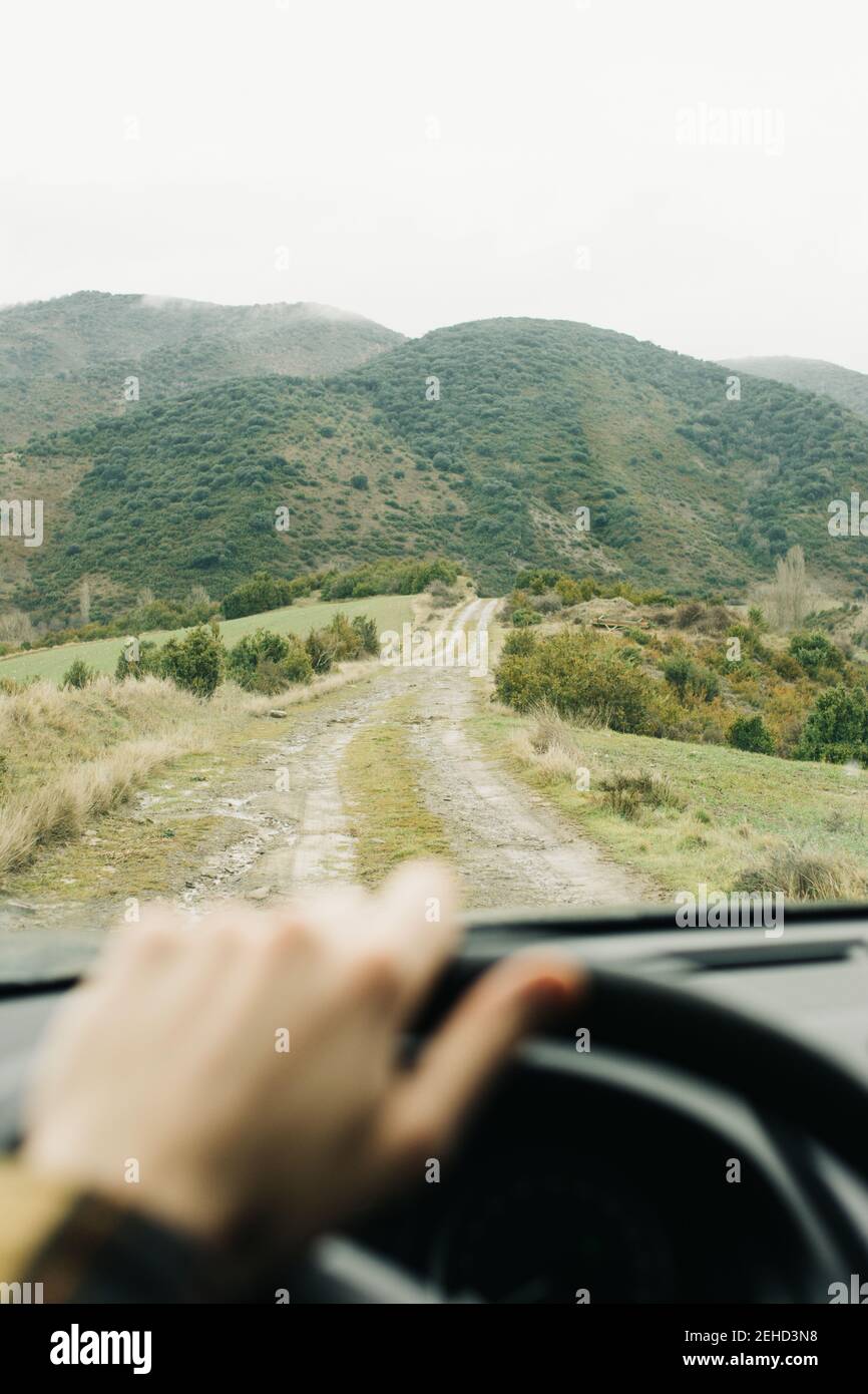 Crop anonymous male tourist driving car along empty rural road towards ...