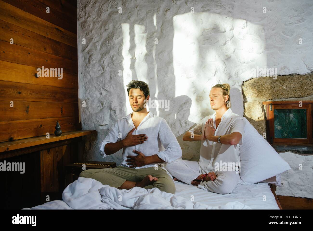 Two friends sitting on a bed while practicing meditation Stock Photo ...