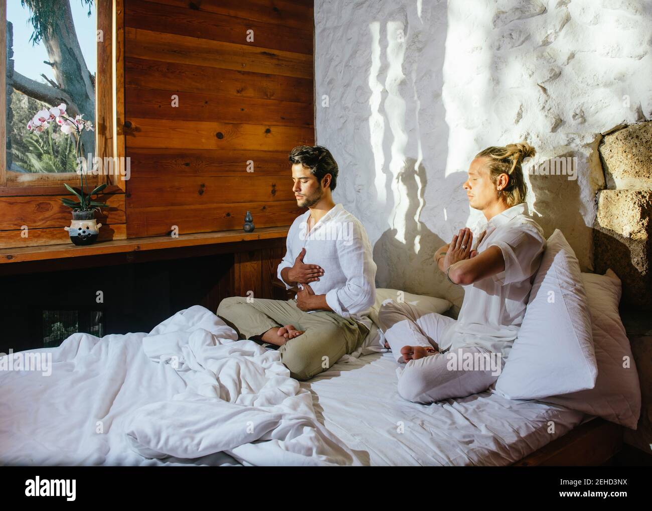 Two friends sitting on a bed while practicing meditation Stock Photo ...
