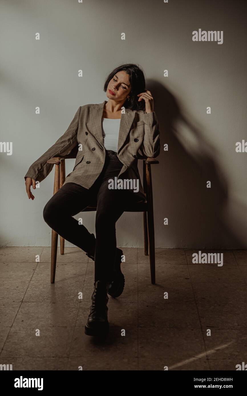 Relaxed female wearing trendy clothes sitting on chair while touching ...