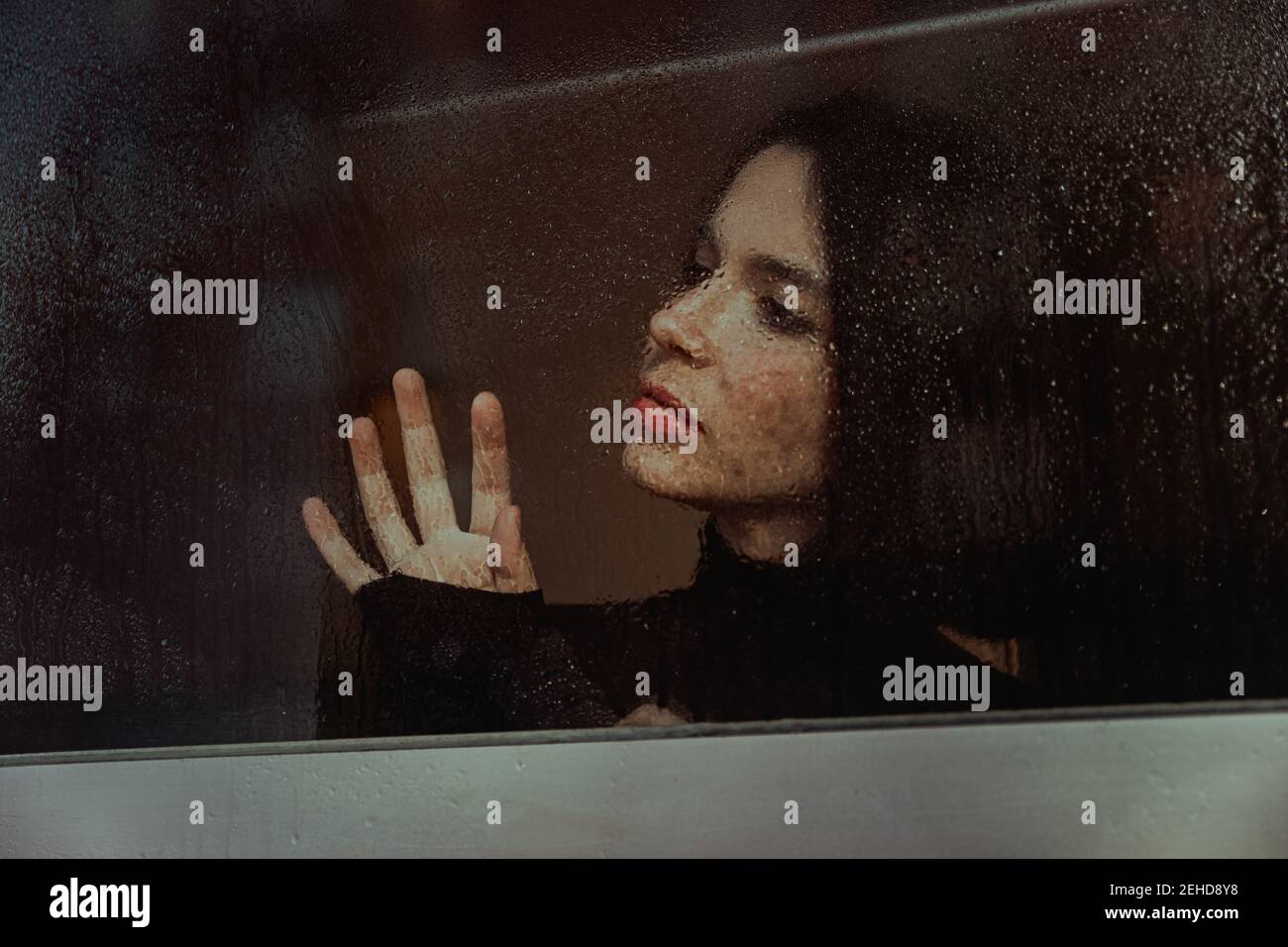 Through glass of thoughtful female standing near window and observing ...