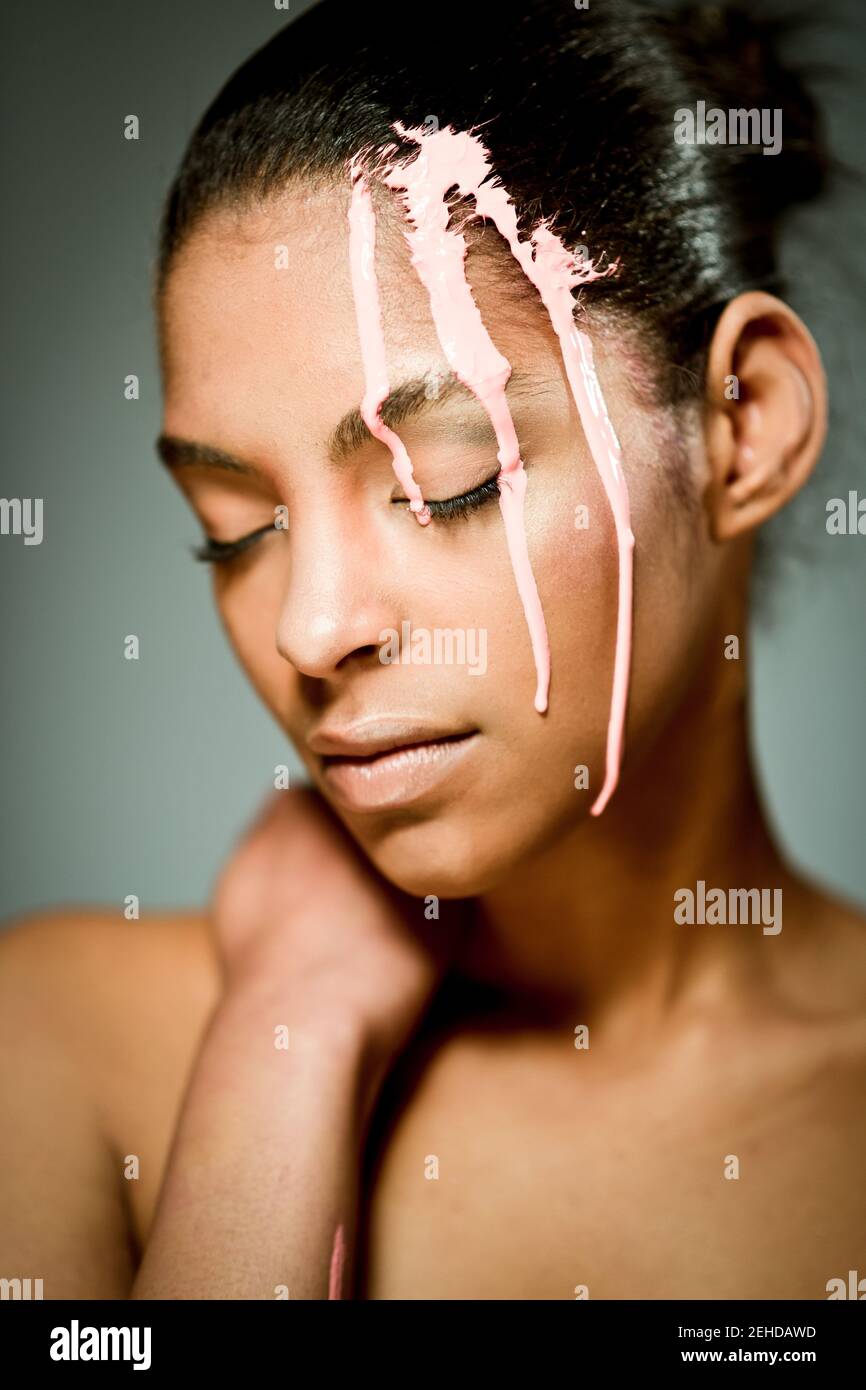 Creative ethnic female model with pink paint dripping on her face with ...