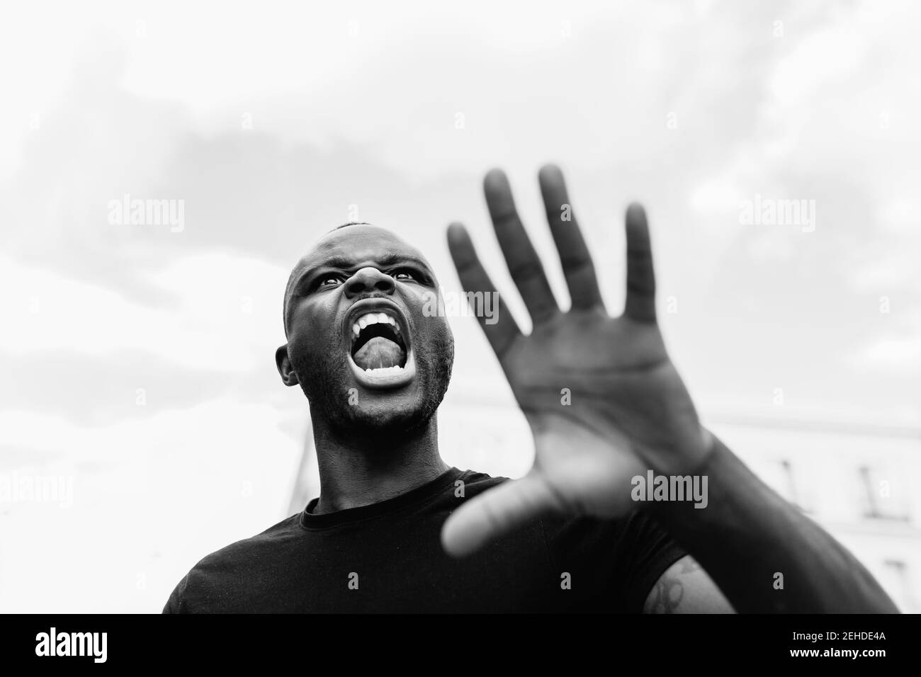 From below black and white of young angry ethnic male screaming and ...