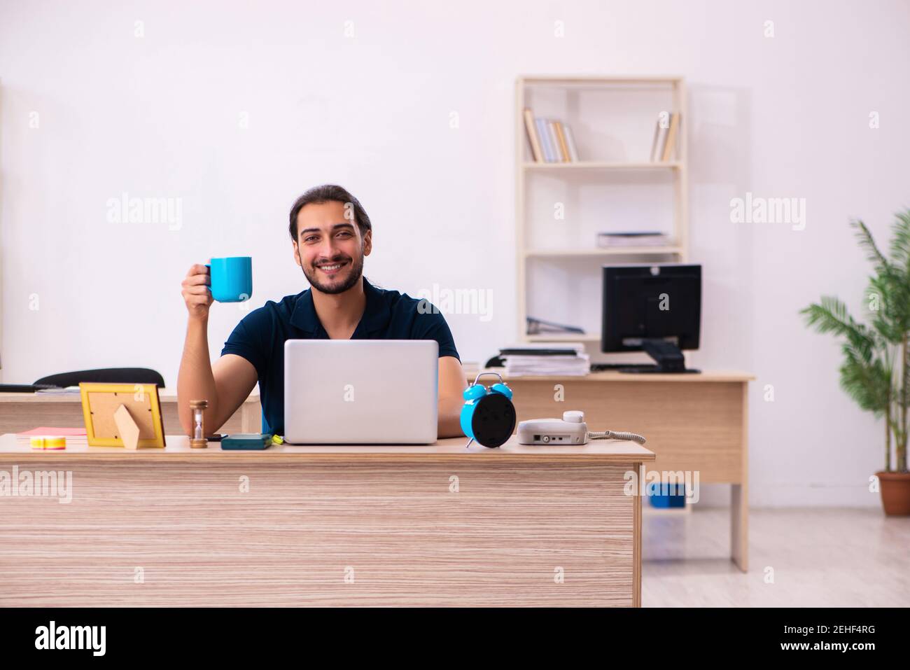 Young employee drinking coffee at workplace Stock Photo - Alamy