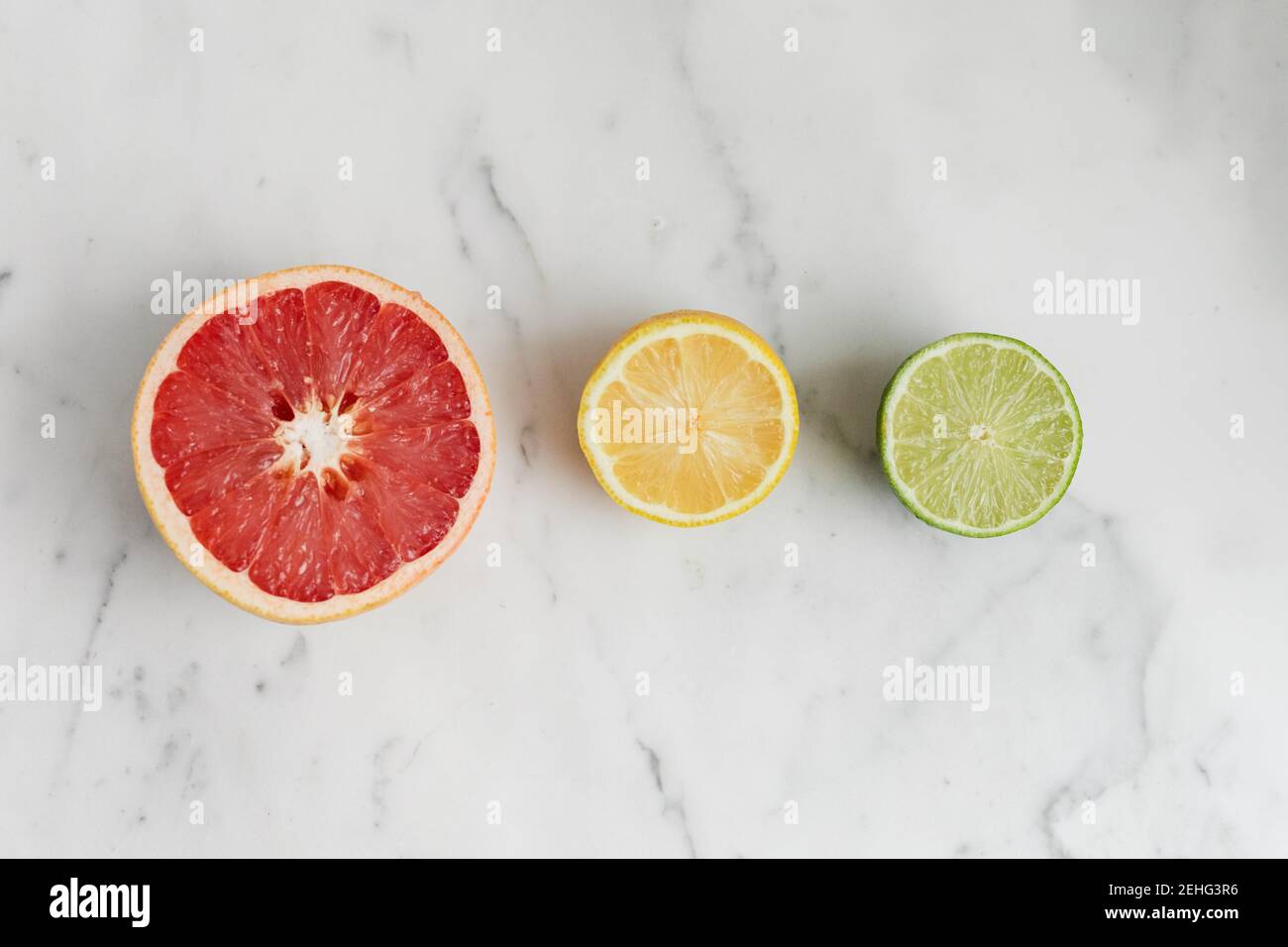 Fresh citrus grapefruit, lemon, and lime, cut on a marble backdrop ...