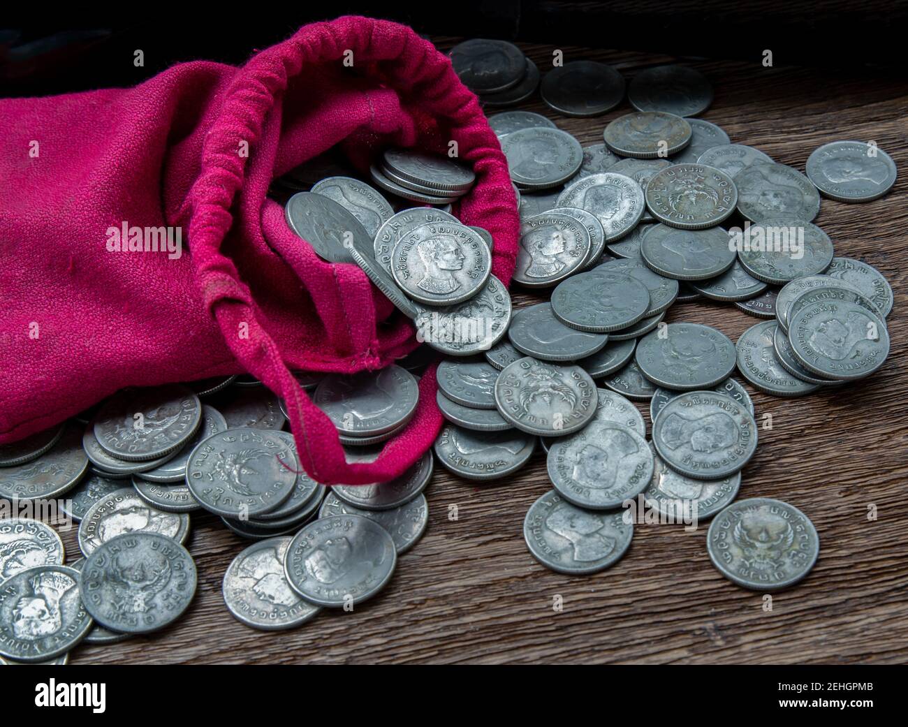 Pile of money coins from red cloth bag on rustic old wooden table ...