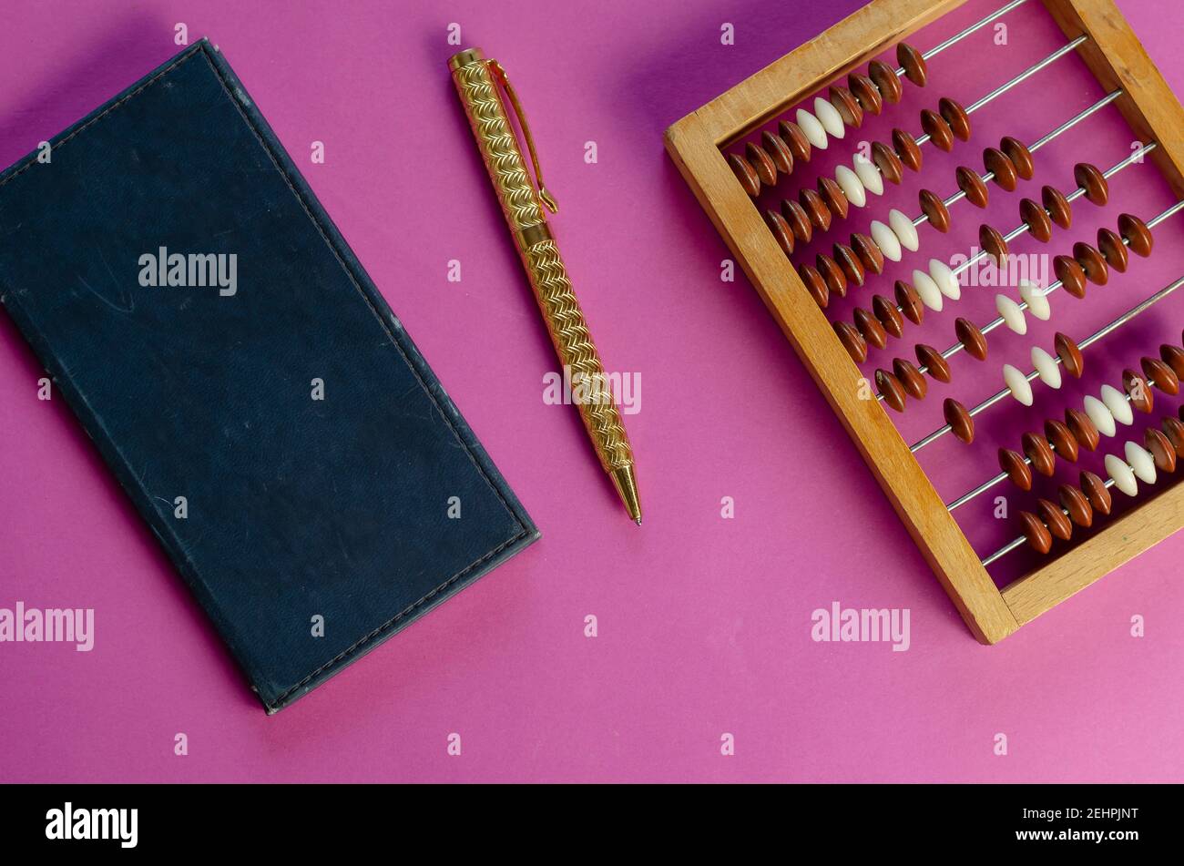 Old notebook, wooden abacus and a gold-colored pen on a pink background ...