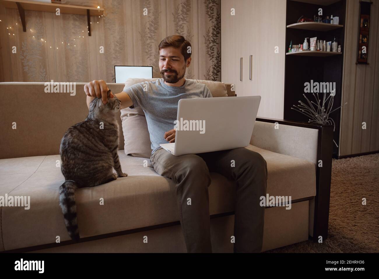 Young attractive smiling guy is browsing at his laptop, sitting at home ...