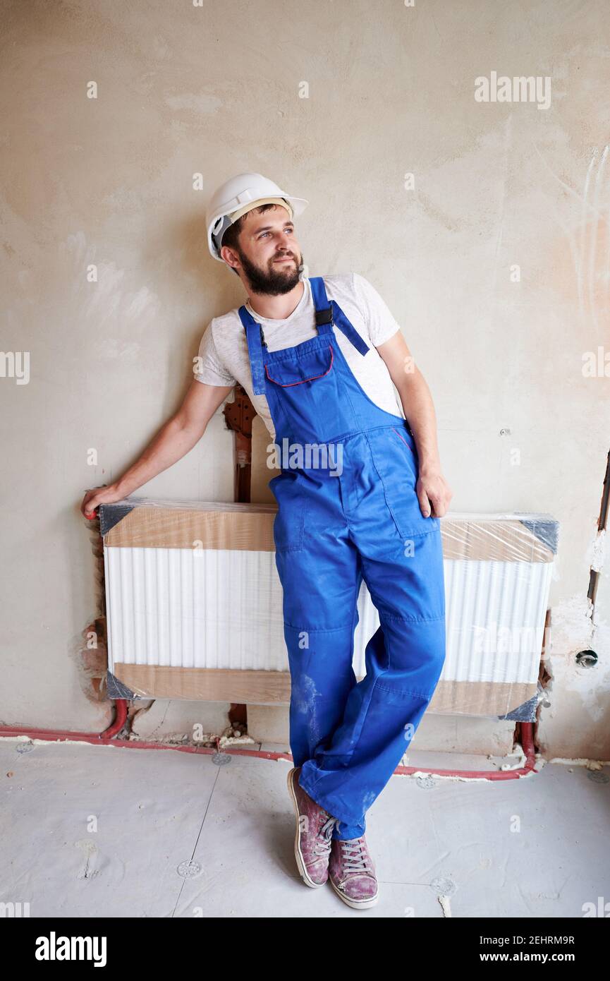 Young bearded plumber, wearing blue overalls, white helmet, standing ...