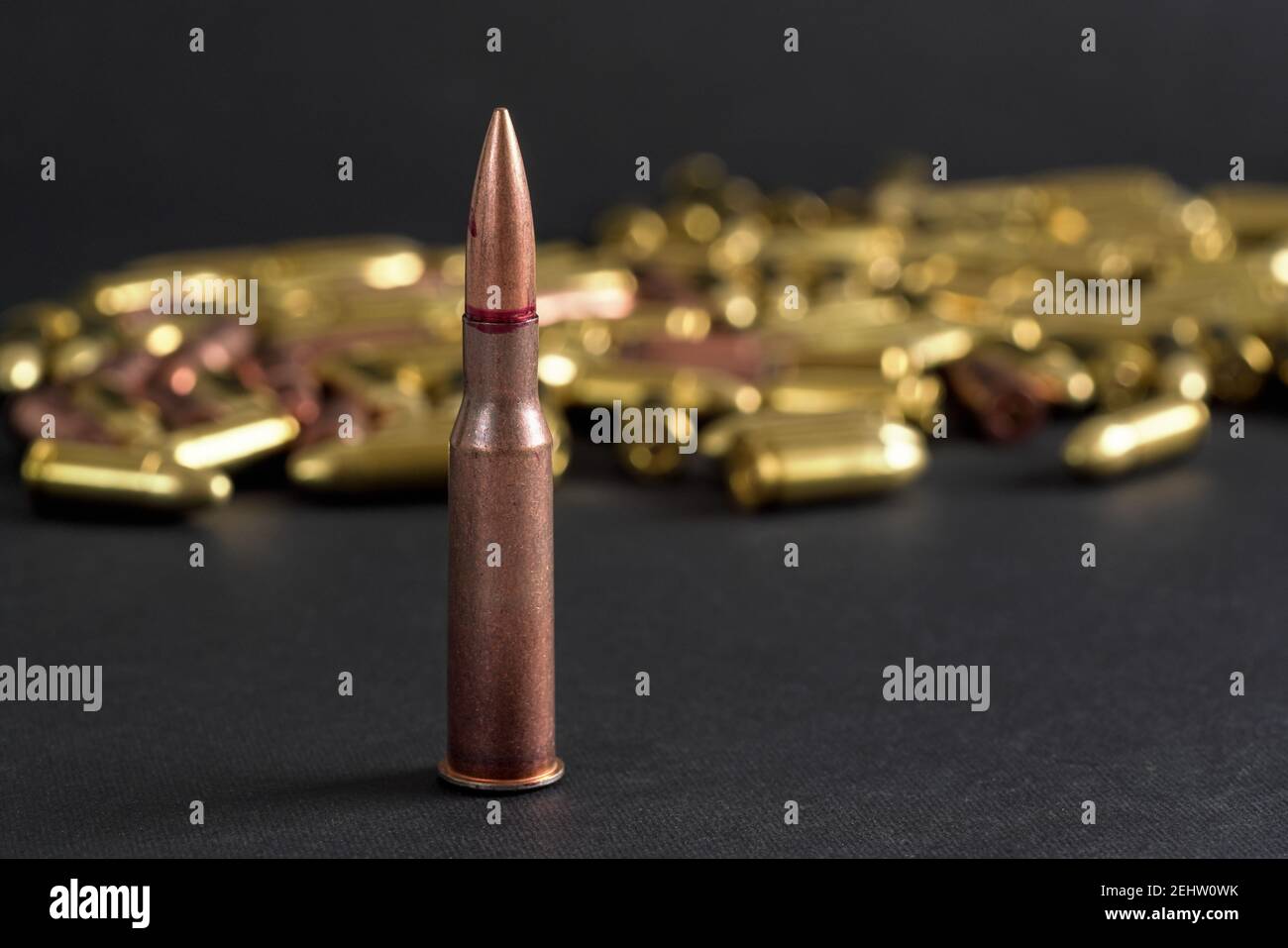 Copper machine gun bullet, more blurred yellow ammo on black board ...