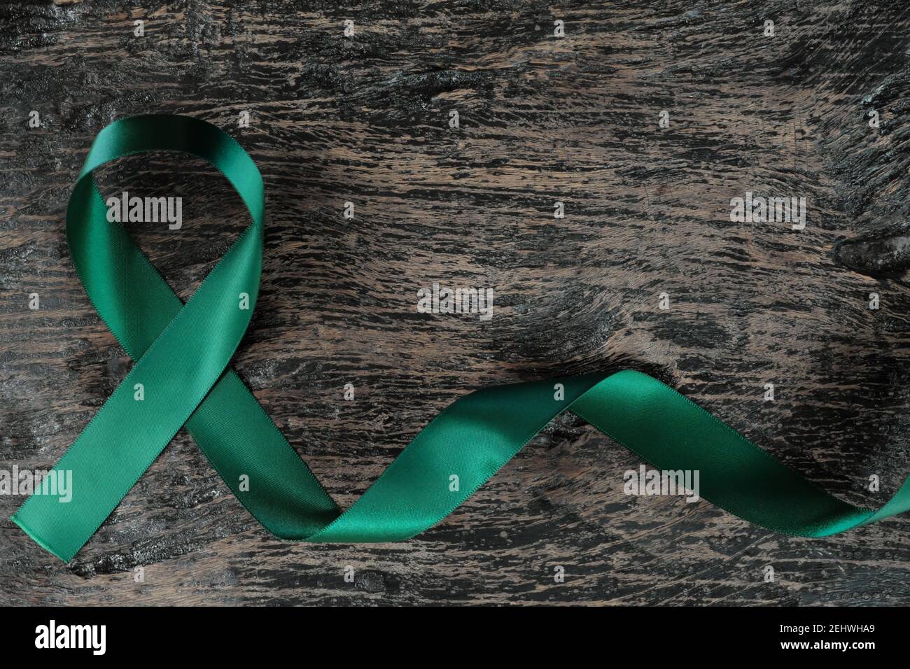 Top view of emerald green ribbon on dark wood background. Liver cancer ...