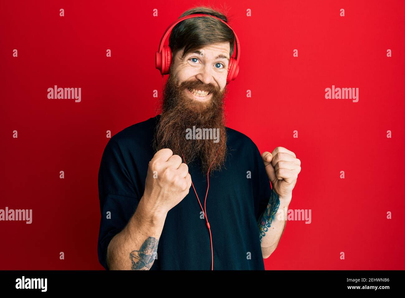 Redhead man with long beard listening to music using headphones excited ...