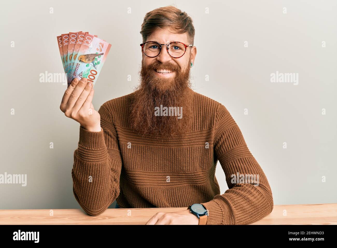 Young irish redhead man holding 100 new zealand dollars banknote ...