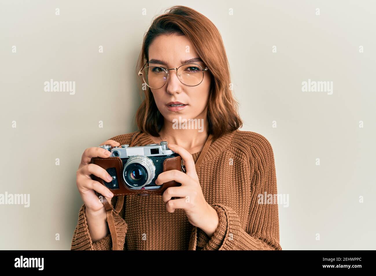 Young caucasian woman holding vintage camera clueless and confused ...