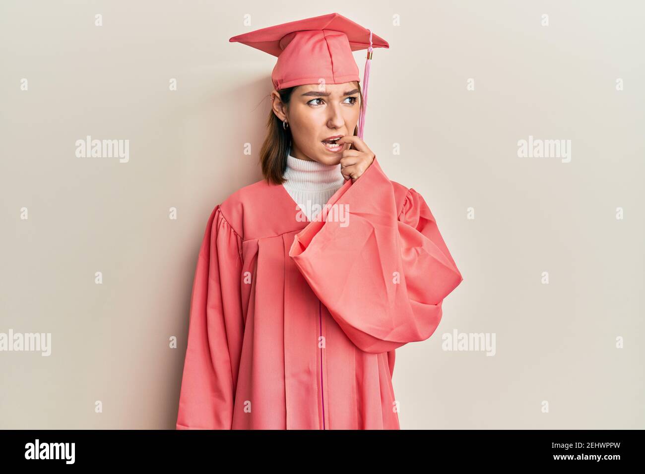 Young caucasian woman wearing graduation cap and ceremony robe looking ...