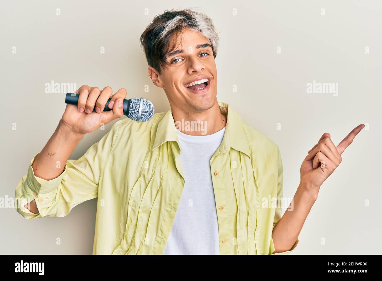 Young hispanic man singing song using microphone smiling happy pointing ...