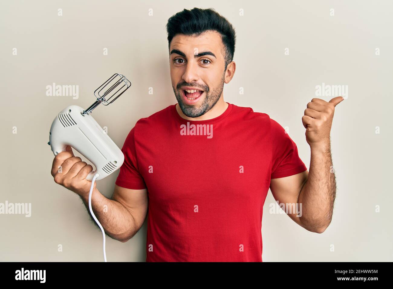 Young hispanic man holding food processor mixer machine pointing thumb ...