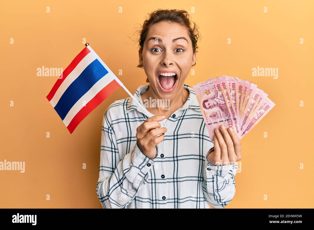 Young brunette woman holding thailand flag and baht banknotes ...