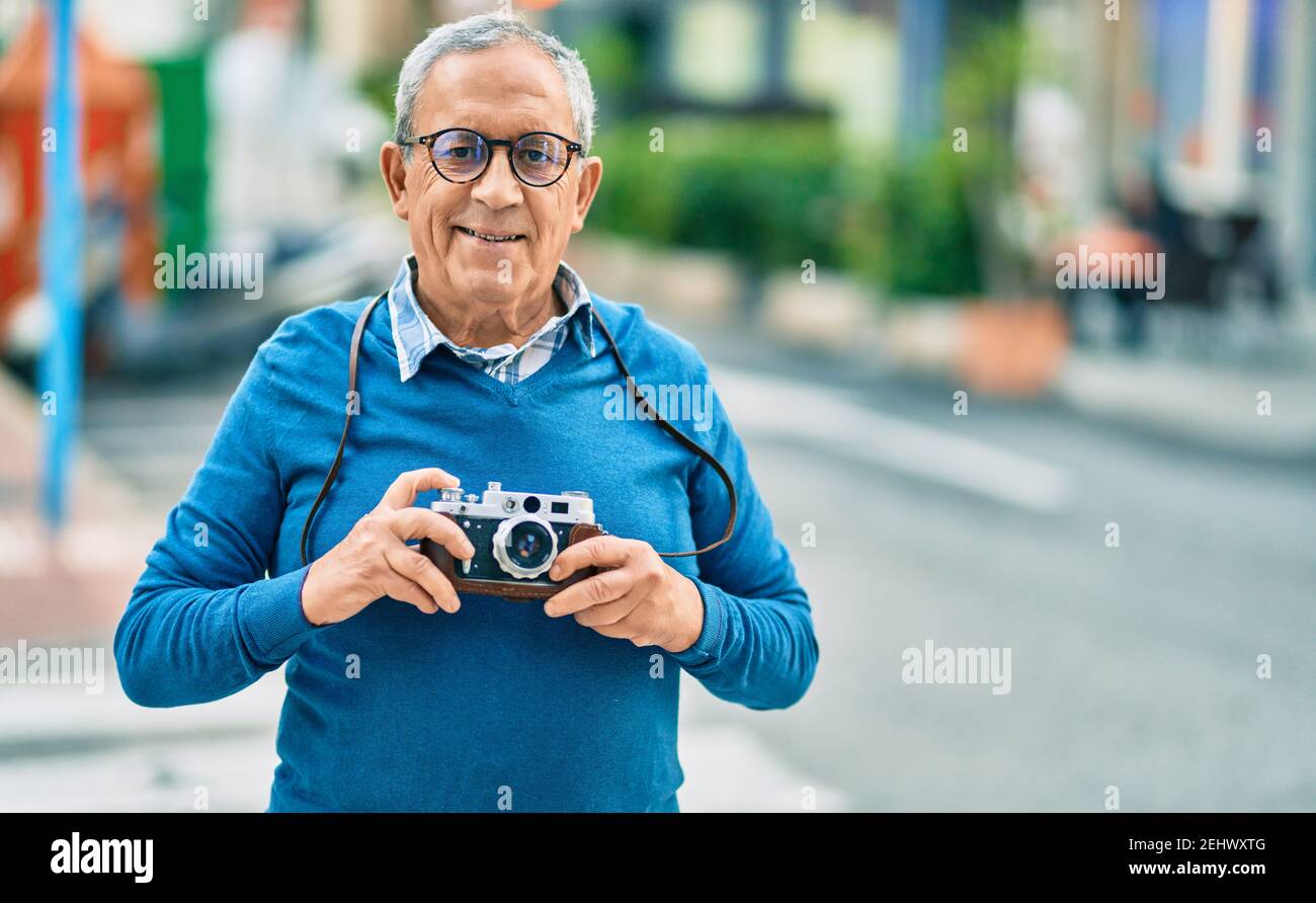 Senior grey-haired tourist man smiling happy using vintage camera at ...