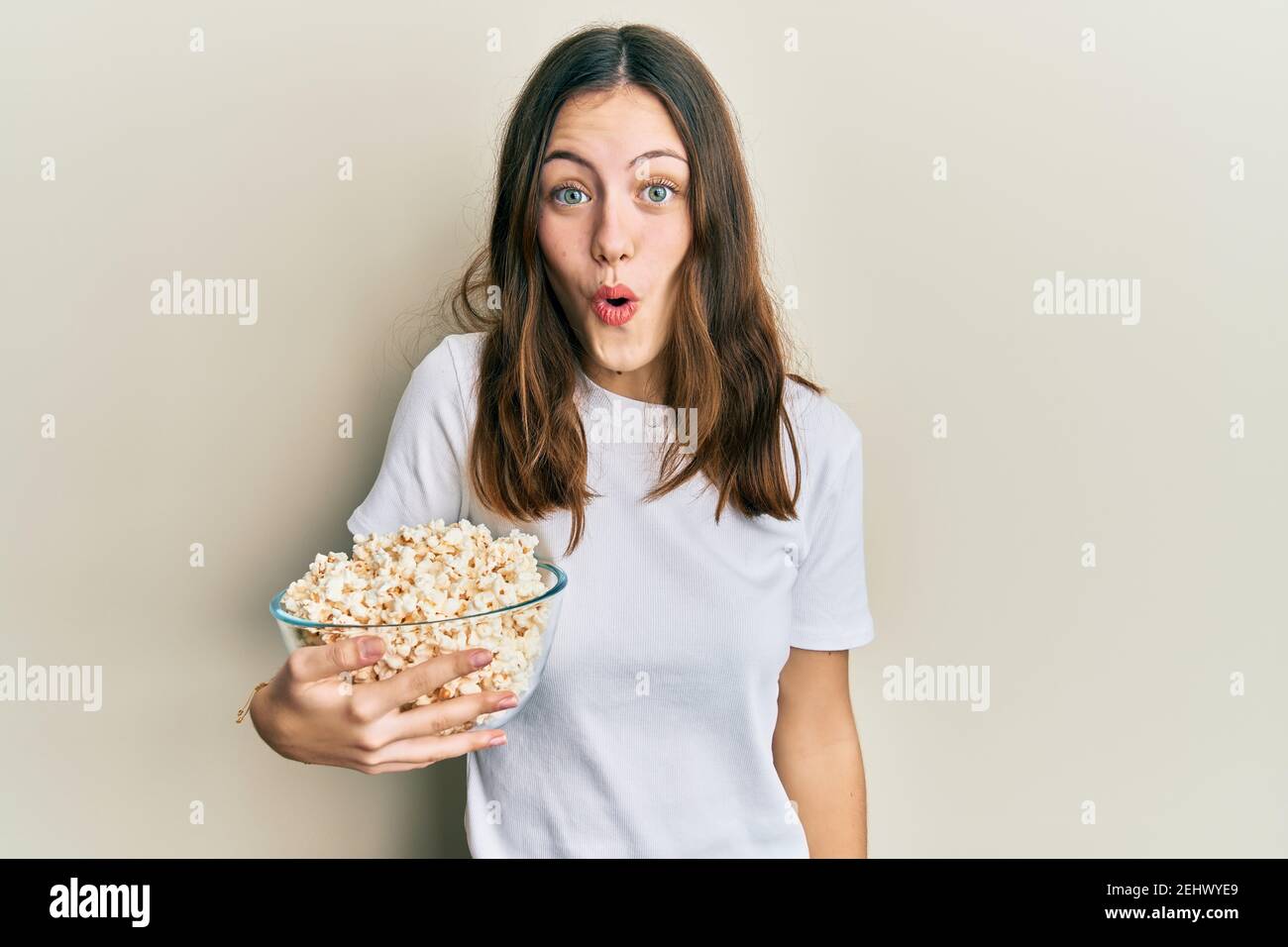 Young brunette woman eating popcorn scared and amazed with open mouth ...