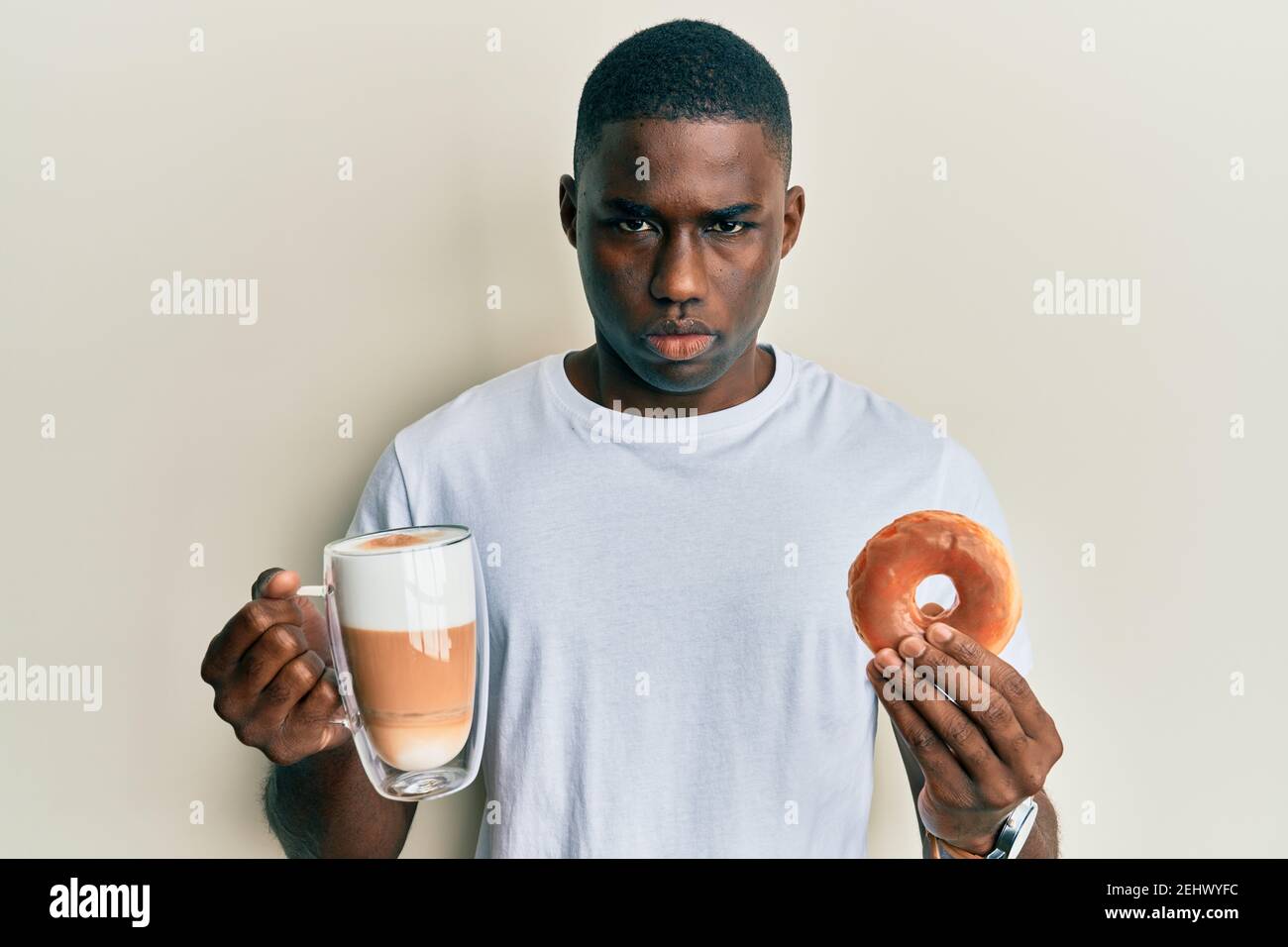 Young african american man eating doughnut and drinking coffee ...