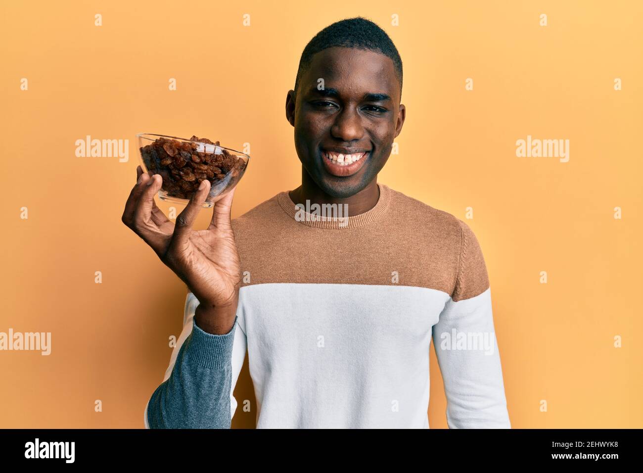 Young african american man holding bowl with raisins looking positive ...