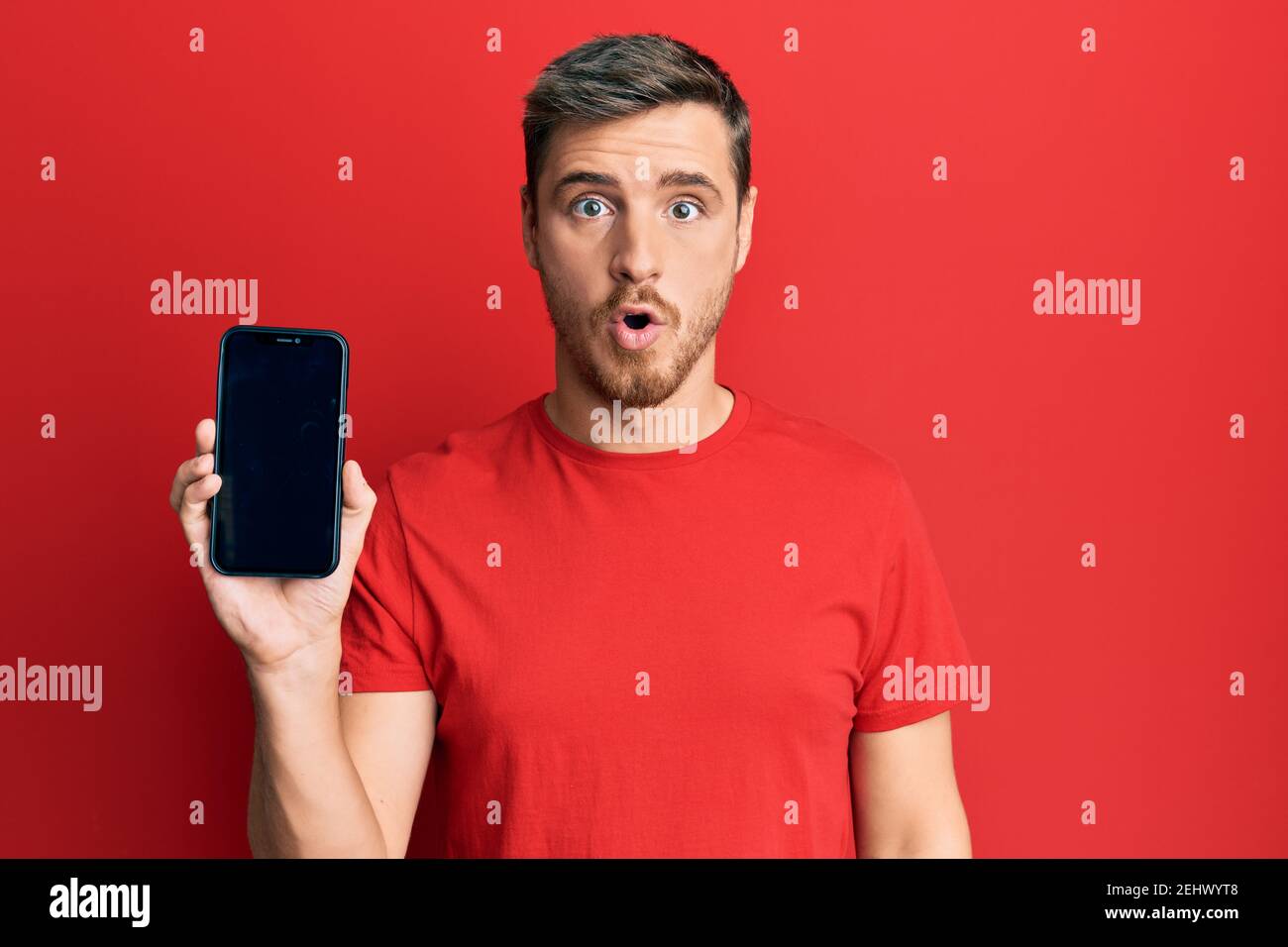 Handsome Caucasian Man Holding Smartphone Showing Screen Scared And