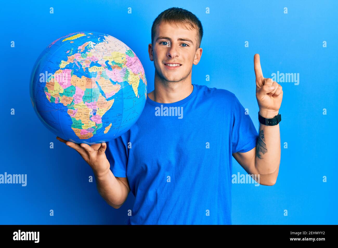 Young caucasian man holding world ball smiling with an idea or question ...