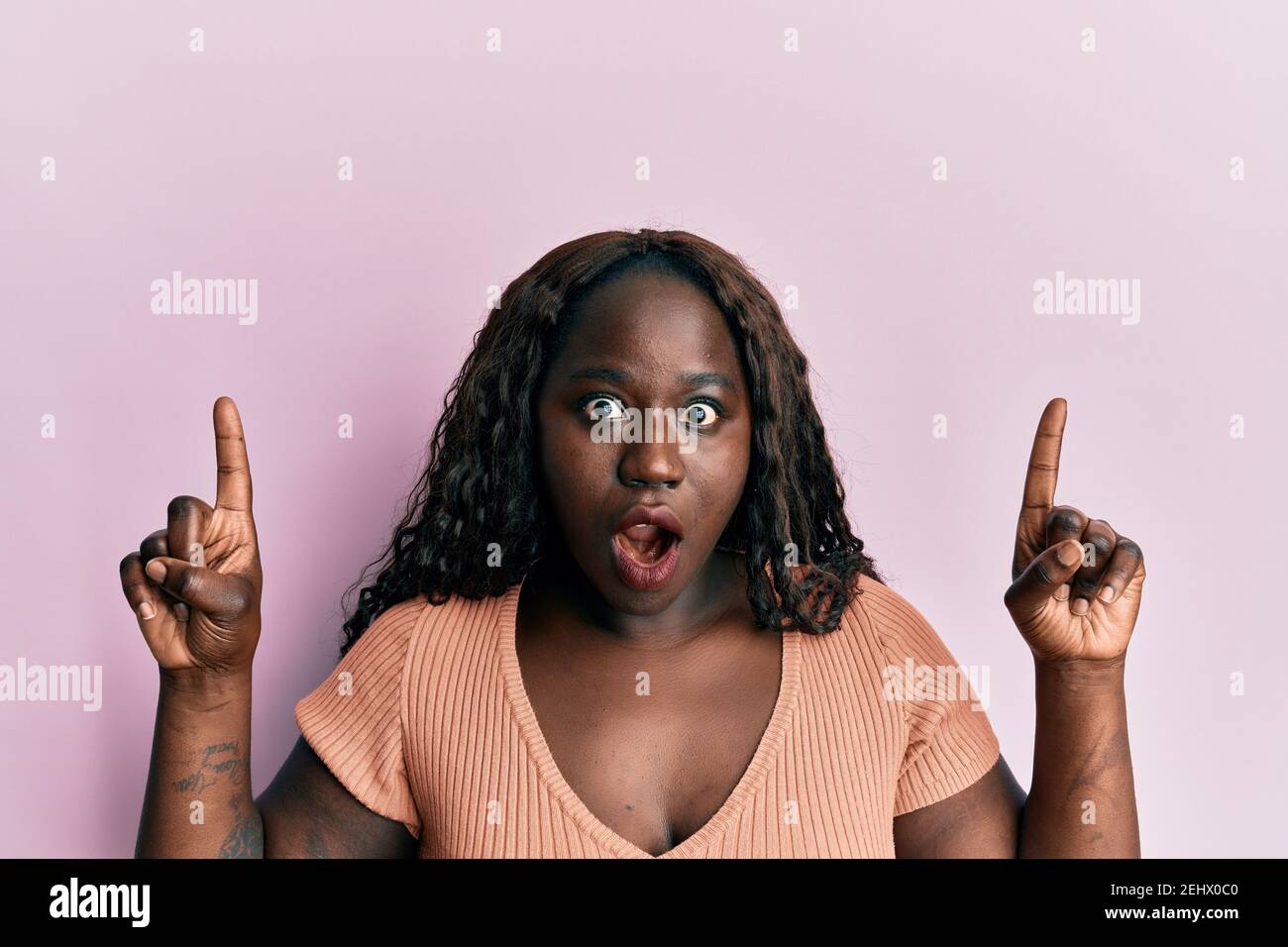 African young woman pointing up with fingers afraid and shocked with ...