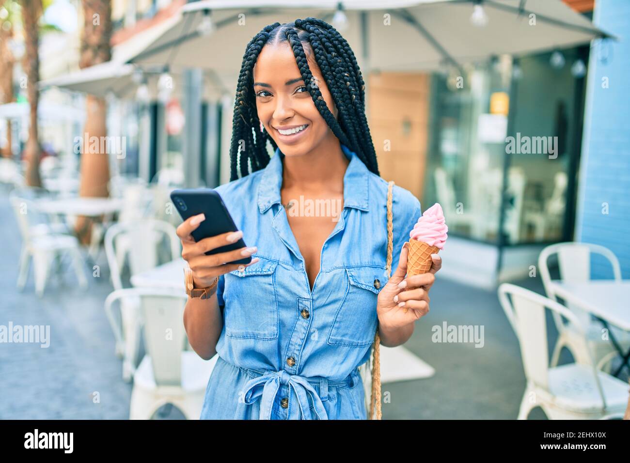 Young african american woman using smartphone and eating ice cream at ...