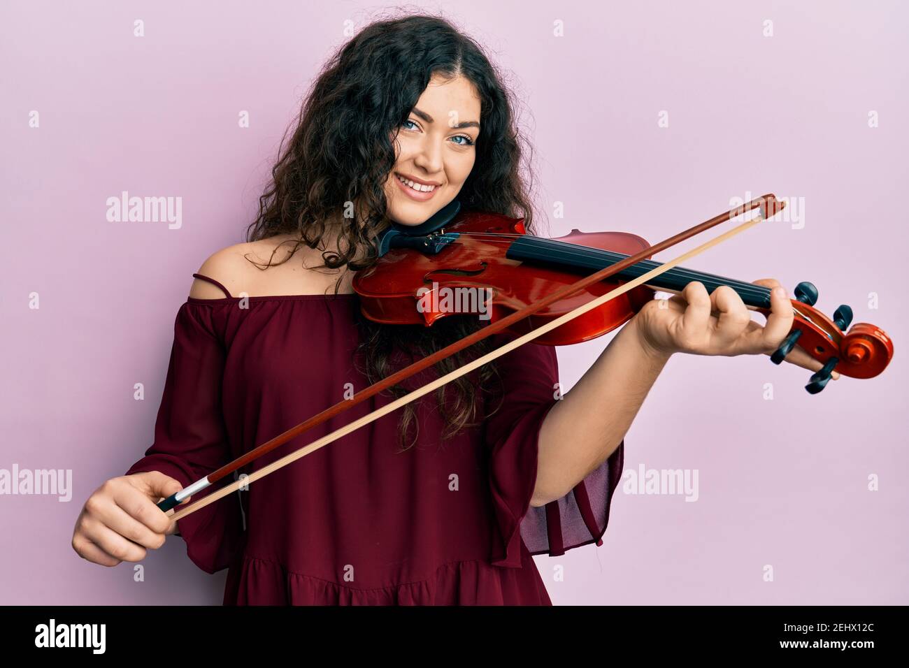 Young brunette musician woman with curly hair playing violin smiling ...
