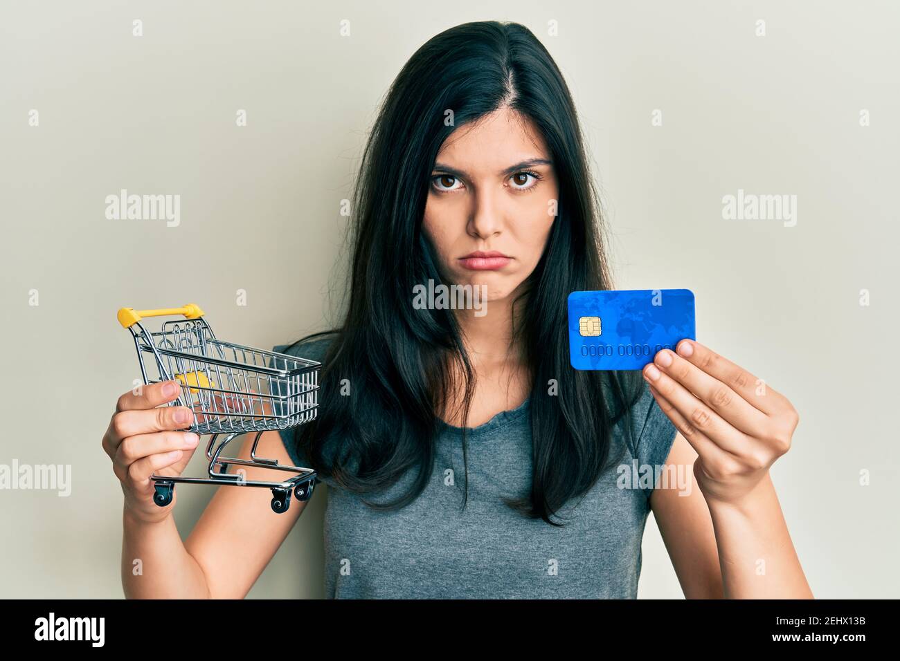 Young hispanic woman holding small supermarket shopping cart and credit ...