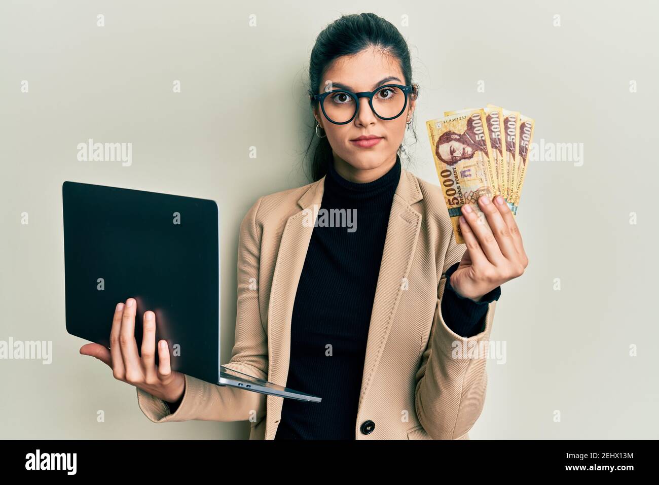 Young hispanic woman wearing business style holding laptop and ...