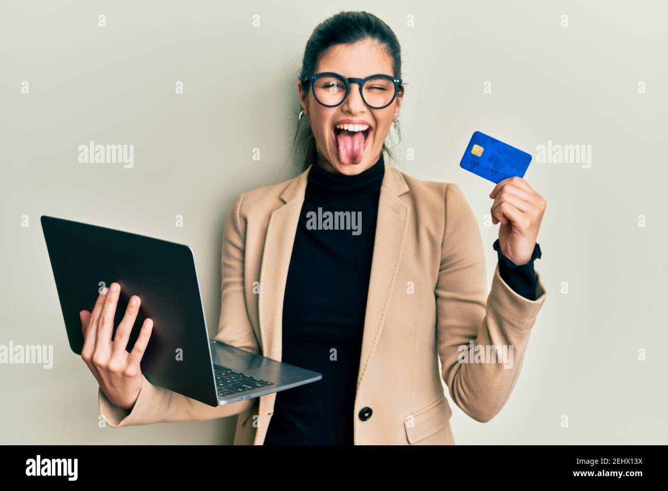 Young hispanic woman wearing business style holding laptop and credit ...